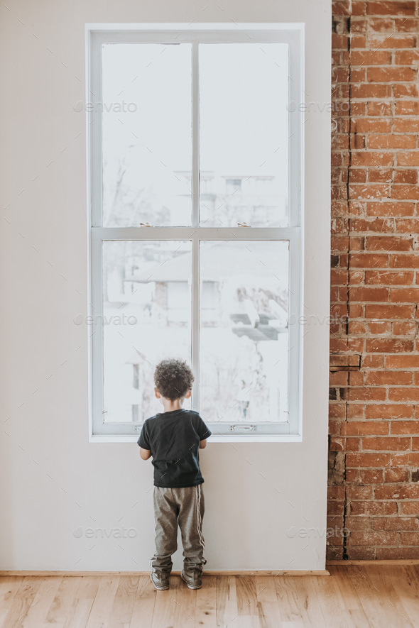 Little boy looking out the window from a home with brick walls and ...