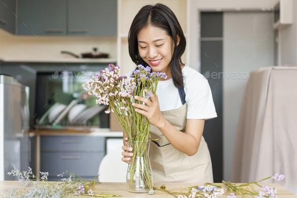 Home lifestyle concept, Young woman take care fresh flowers in vase on table in kitchen room ...