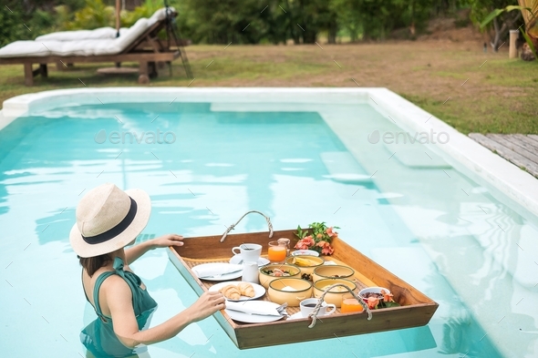 woman having Floating Breakfast in luxury pool hotel, girl with hat ...