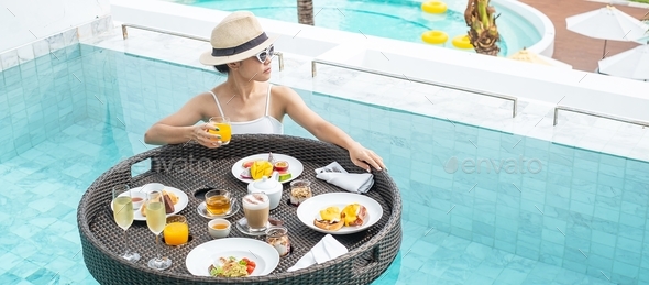 woman having floating breakfast in swimming pool Stock Photo by JoPanwatD