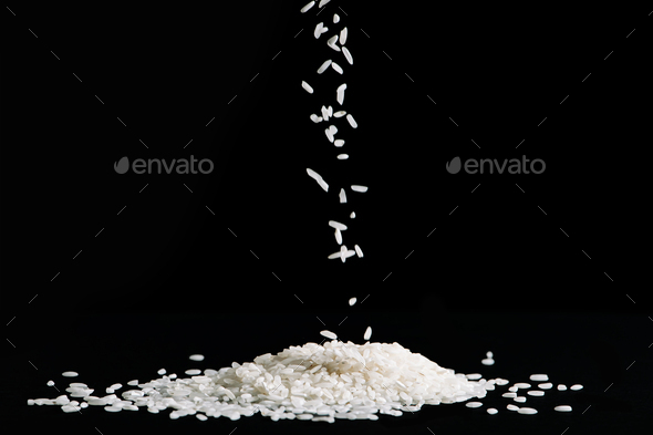 Raw white rice is falling on table. Pile of uncooked long rice on black ...