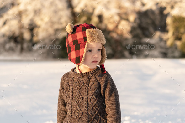 Boy wearing a sweater and bomber hat in the snow at sunset Stock Photo ...