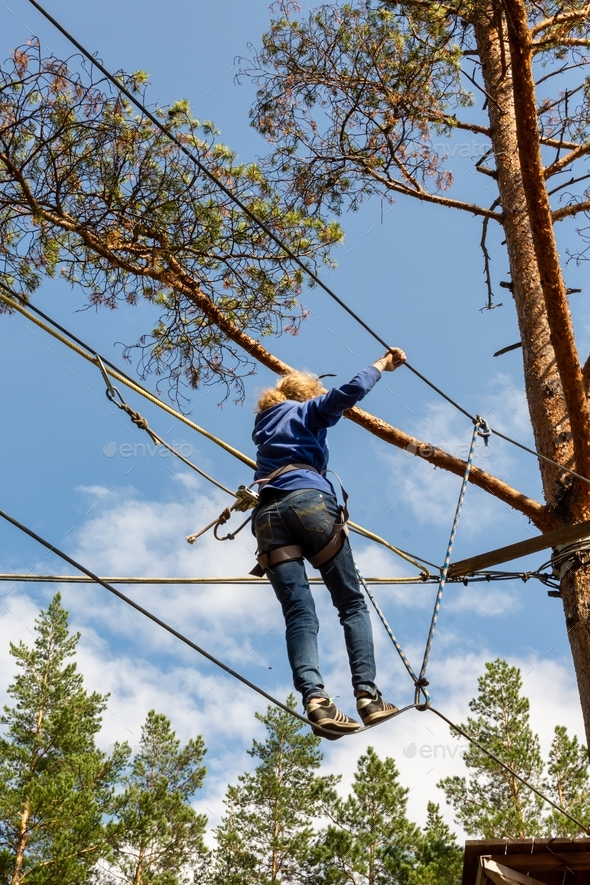 A young woman walks on a rope obstacle course in the forest and trains ...