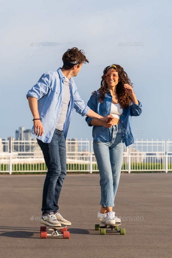 Stylish couple skateboarding together over urban skyline. Young adult ...