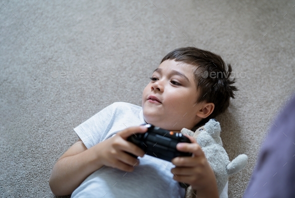boy lying on carpet holding video game or game console. Smiling Child ...