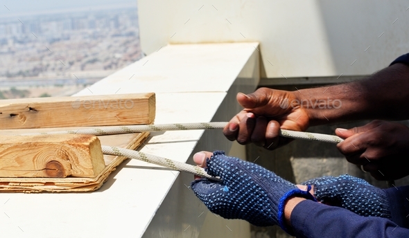Two unrecognizable diverse men pull ropes together on the rooftop of a ...