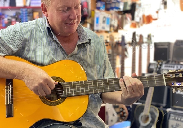 Middle aged happy baby boomer male musician playing guitar in a music ...