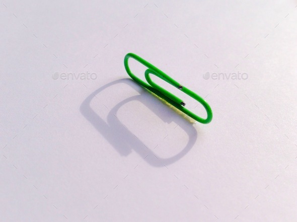 Green metallic metal paper clip on edge by itself macro with shadow ...