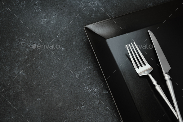 Cutlery and black square dish on dark textured background. Table ...