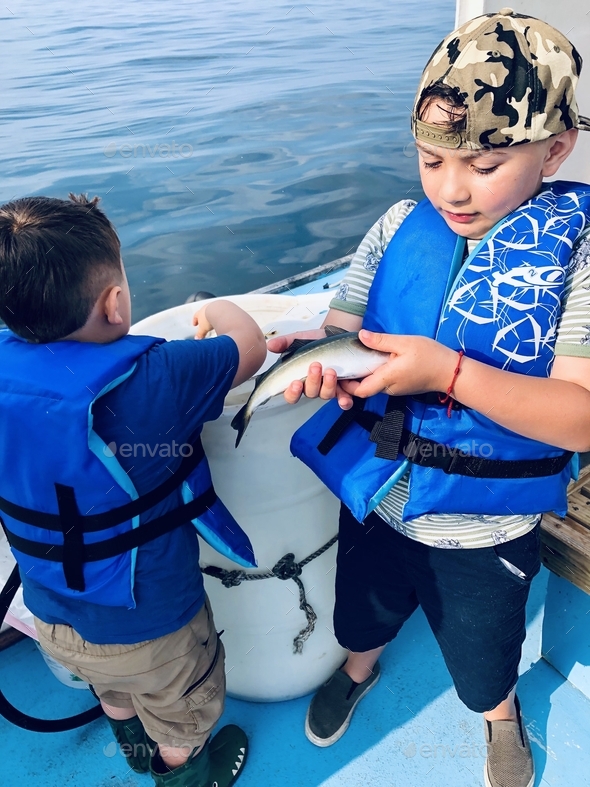 Two brothers on a fishing boat holding bait fish. Stock Photo by marisap7