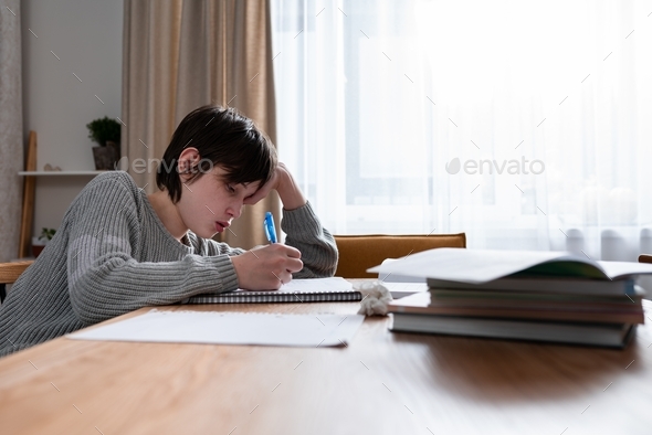 Unhappy teenager boy doing school lessons at home. Problems and ...