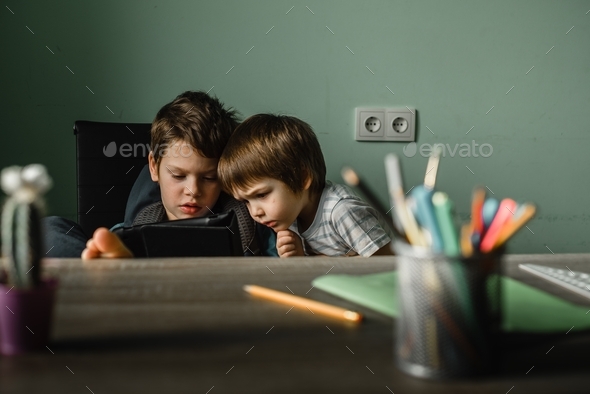 Junior boy with his brother playing tablet at home, growing up with ...