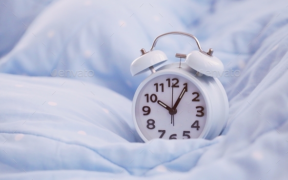 Alarm clock on bed with blue blanket closeup cozy bedroom blur macro ...