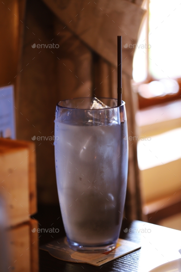 Cold glass of water with ice and straw closeup on table near window ...