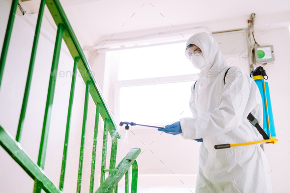 Man in Hazmat suit, protective gloves and goggles use sprayer equipment ...
