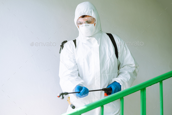 Man in Hazmat suit, protective gloves and goggles use sprayer equipment ...