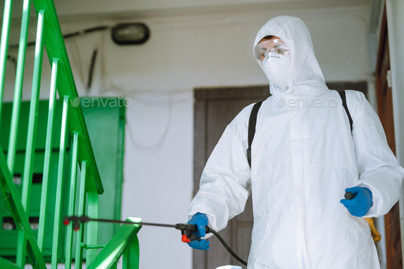 Man in Hazmat suit, protective gloves and goggles use sprayer equipment ...