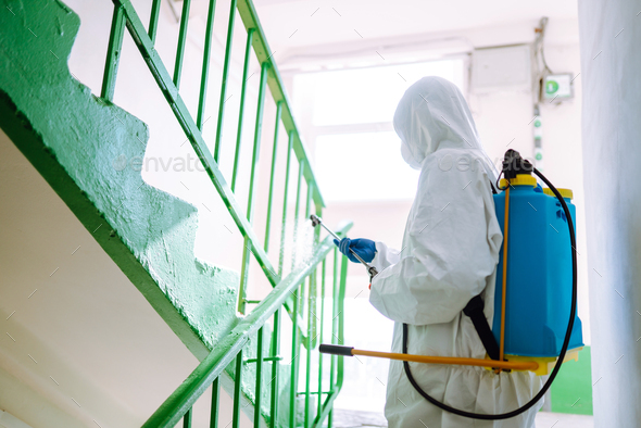 Man in Hazmat suit, protective gloves and goggles use sprayer equipment ...
