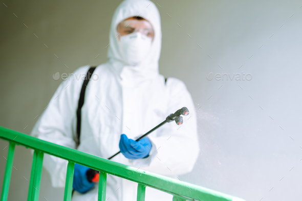 Man in Hazmat suit, protective gloves and goggles use sprayer equipment ...