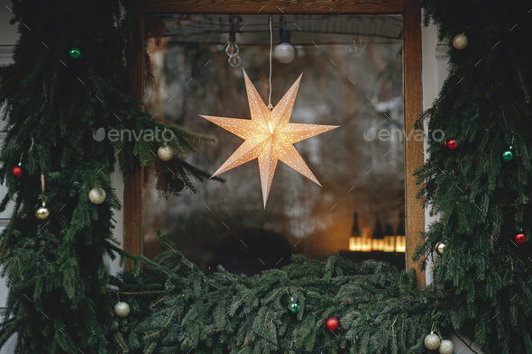 Stylish illuminated christmas star in window and fir branches with ...