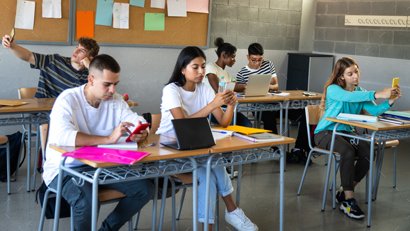 Multiracial high school students distracted from lesson using mobile ...