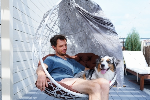 Adult man sitting in hanging chair with furry friend Aussie shepherd ...
