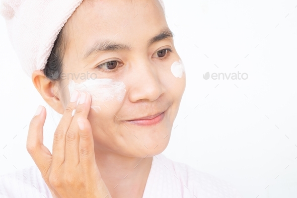 Woman applying lotion skin serum cream on face with smile after shower ...