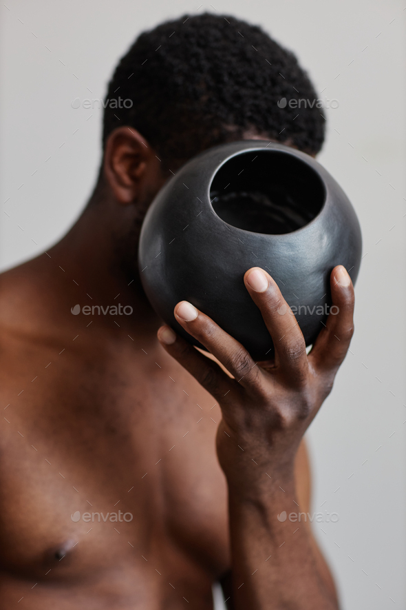 Black man holding round tan vase and hiding face, nature in design ...