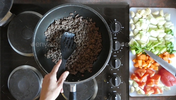 cropped hand holding spoon stirring food cooking mince meat in pan on ...