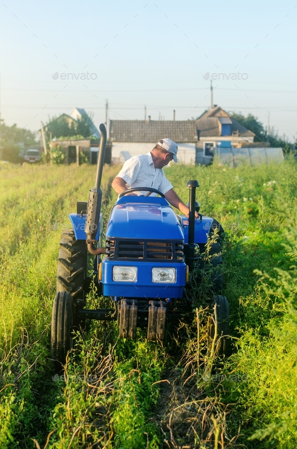 A farmer on a tractor drives across the farm field and harvests ...