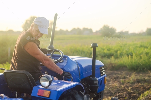 A farmer on a tractor drives across the farm field. Agricultural ...