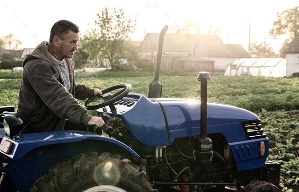 Farmer driving a tractor across the field. Stock Photo by iLixe48