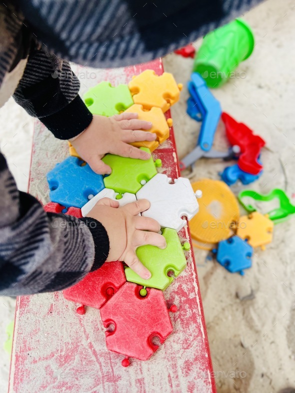 The child plays in the sandbox with colorful puzzles. Stock Photo by ...