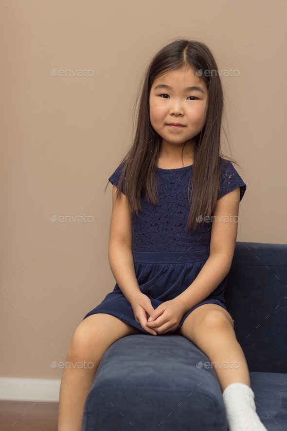 Female portrait of little smiling girl, cute adorable asian relaxed child on couch looking at ...