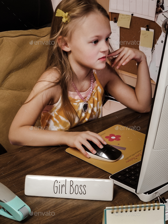 A little girl sits at an office desk with a white nameplate that reads ...