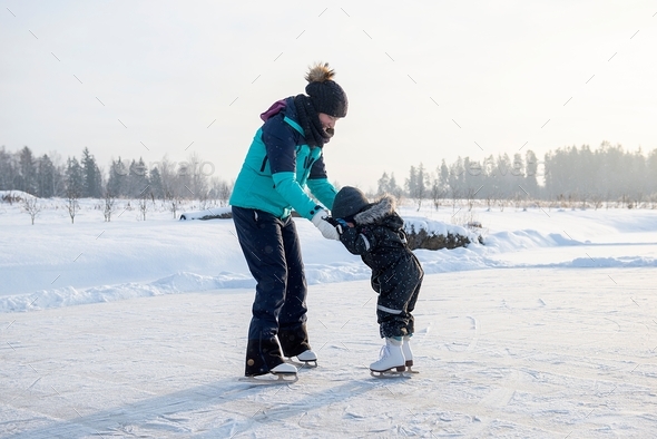 Young mother teaching her little baby boy son ice skating at outdoor ...