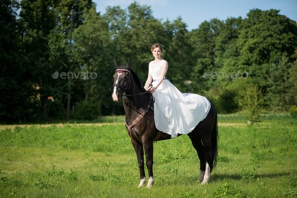Beautiful and stunning bride, riding a horse in the nature, on her ...