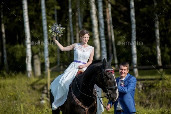 A young couple-bride and groom go horseback riding in nature on their ...