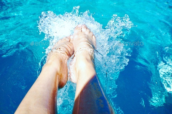Woman splashing feet in pool on summer day. Stock Photo by Mrskiac