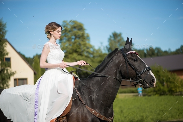 Beautiful and stunning bride, riding a horse in the nature, on her ...
