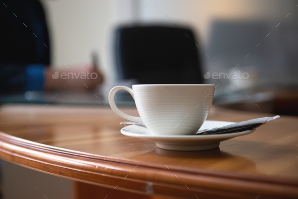 white cup of coffee on an office desk in a conference room, business ...