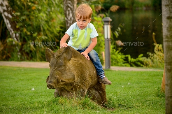 a boy sits on a sculpture of a wooden boar in the park Stock Photo by ...