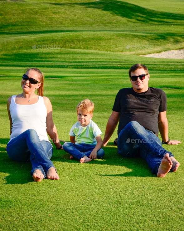 young parents with a child are sitting on a green lawn. family picnic ...