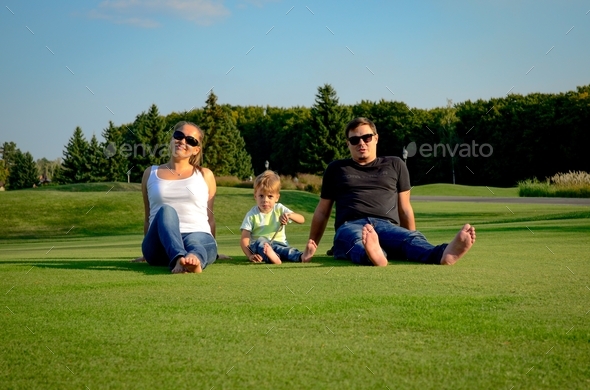 young parents with a child are sitting on a green lawn. family picnic ...