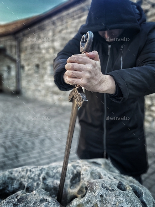 the sword in the stone of King Arthur - Clarent. a man in black drags ...