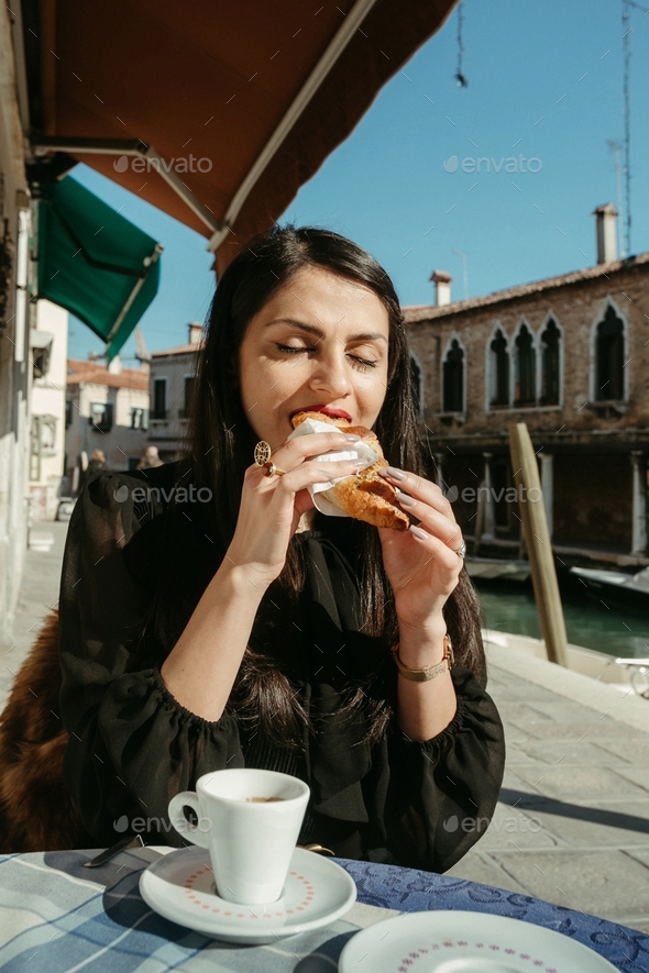Young woman eating cornetto and drinking coffee in a street bar in ...