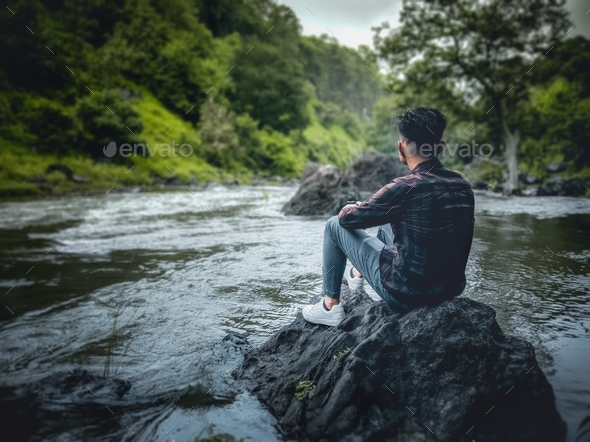 Boy sitting on a rock in middle of the river Stock Photo by nitinkushwah880