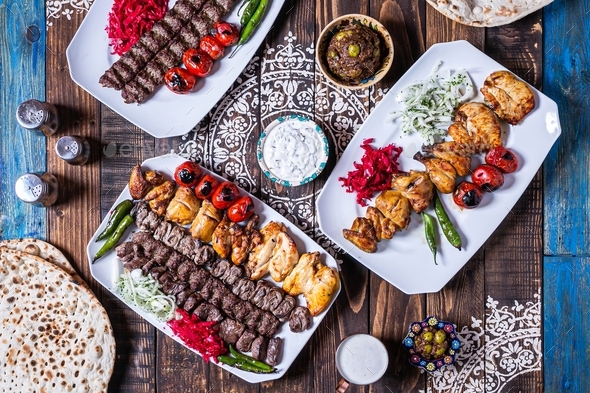 Flat lay Persian table with a mix of kebabs, traditional bread, and ...