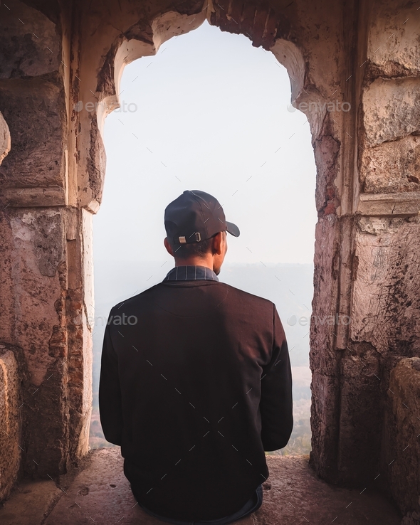 Boy sitting on the window of an ancient Indian structure and looking at ...