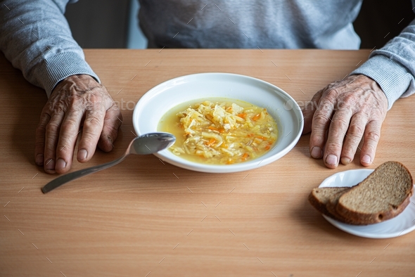 View from above of a soup plate, bread and the untidy hands of an old ...